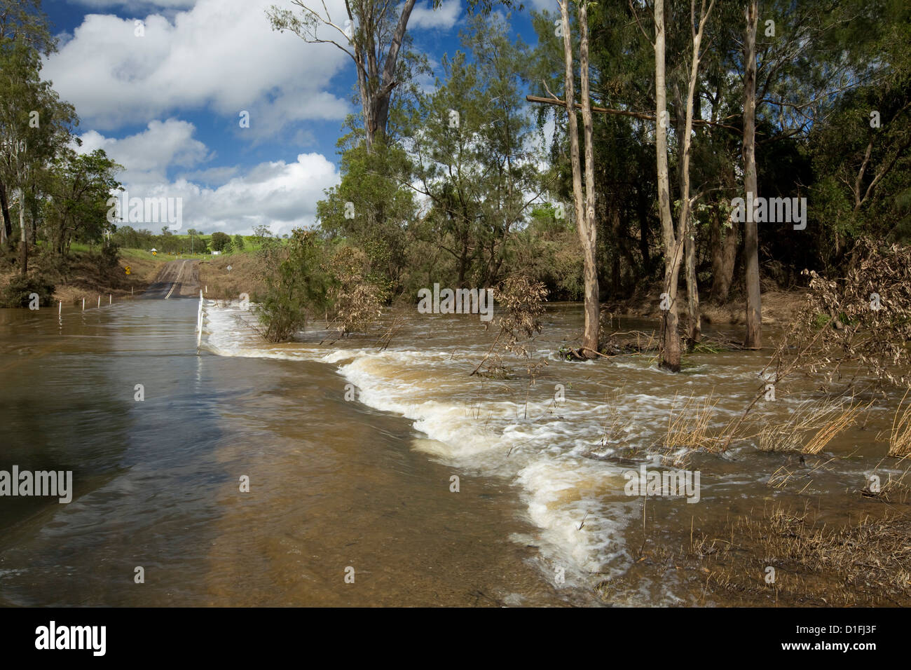 Water of flooding river running across concrete causeway of rural road ...