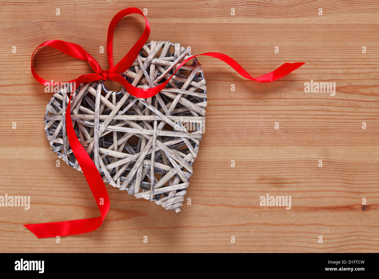 A heart shaped wicker decoration with red ribbon on a rustic wooden ...