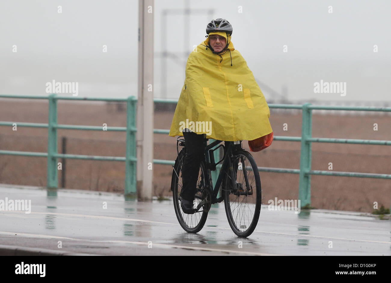 A cyclist in a bright yellow poncho cycles along Brighton seafront in ...