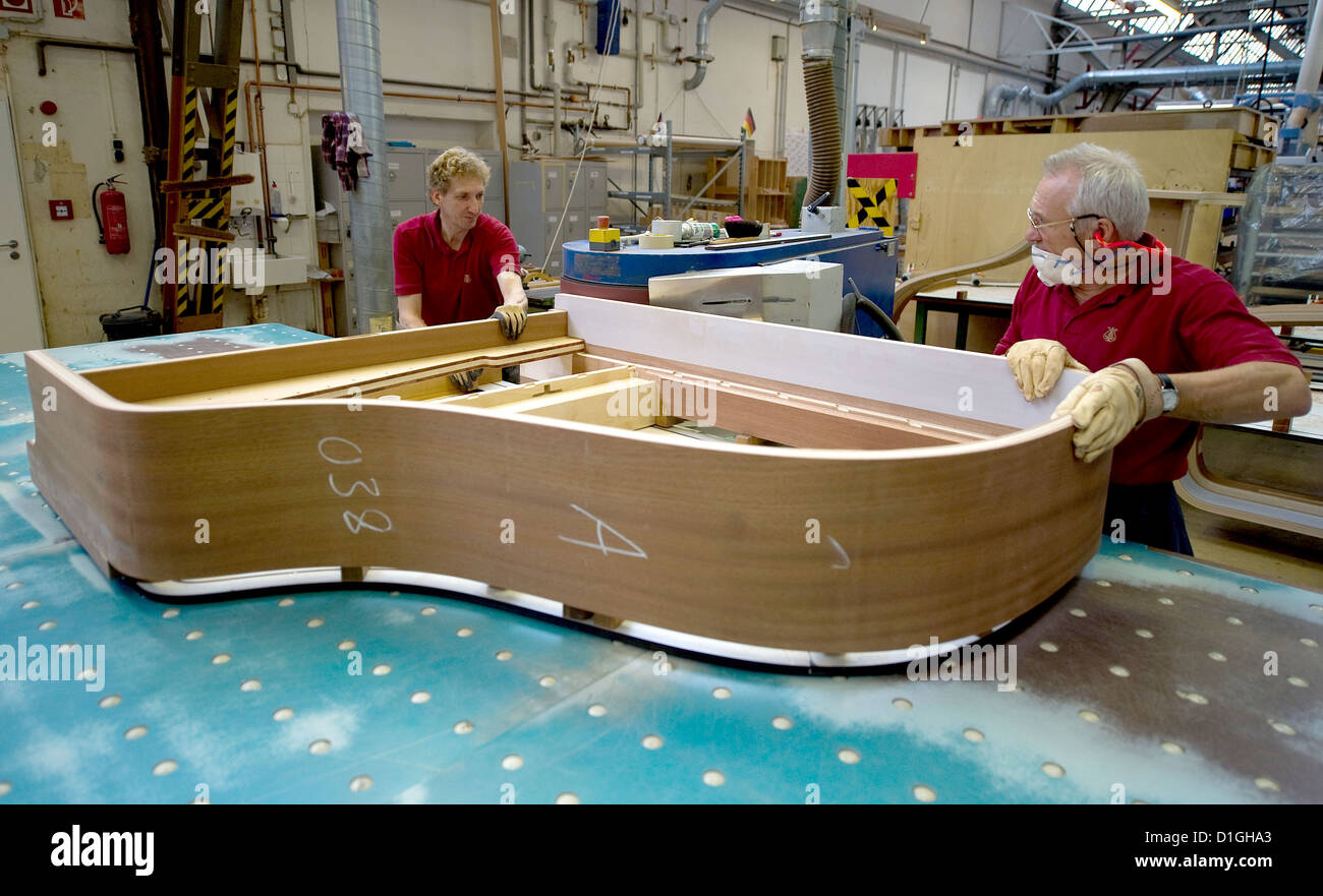 Two craftsmen work on the frame of a grand piano at piano manufacturer ...