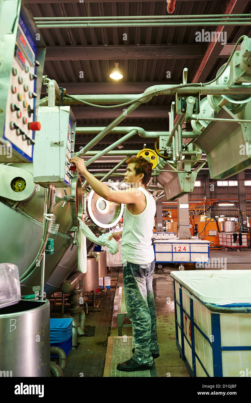 A strong worker poses and inspects fabric next to large dying machines ...