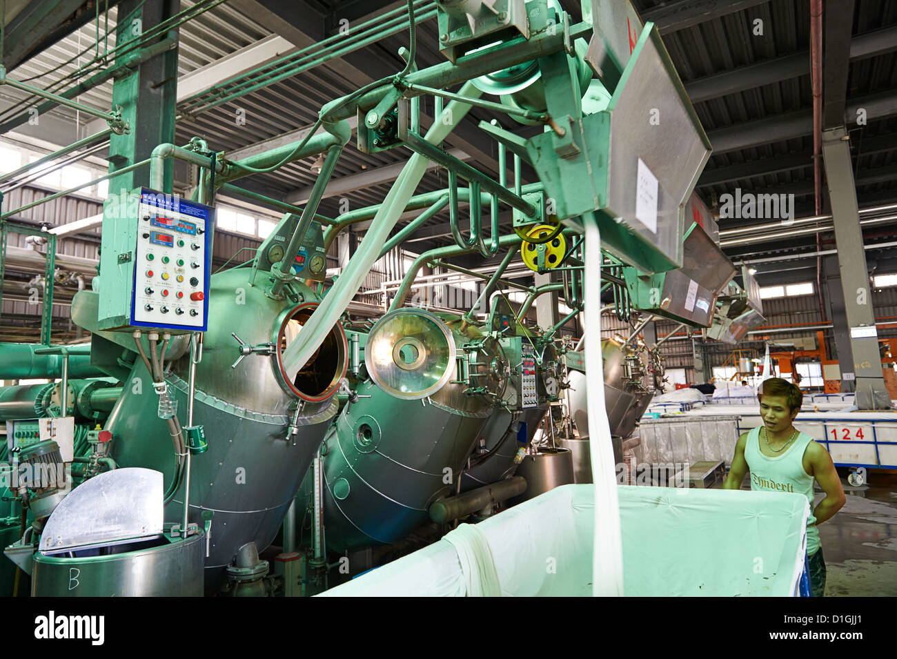 A strong worker poses and inspects fabric next to large dying machines ...