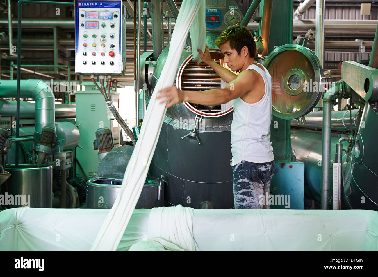 A strong worker poses and inspects fabric next to large dying machines ...