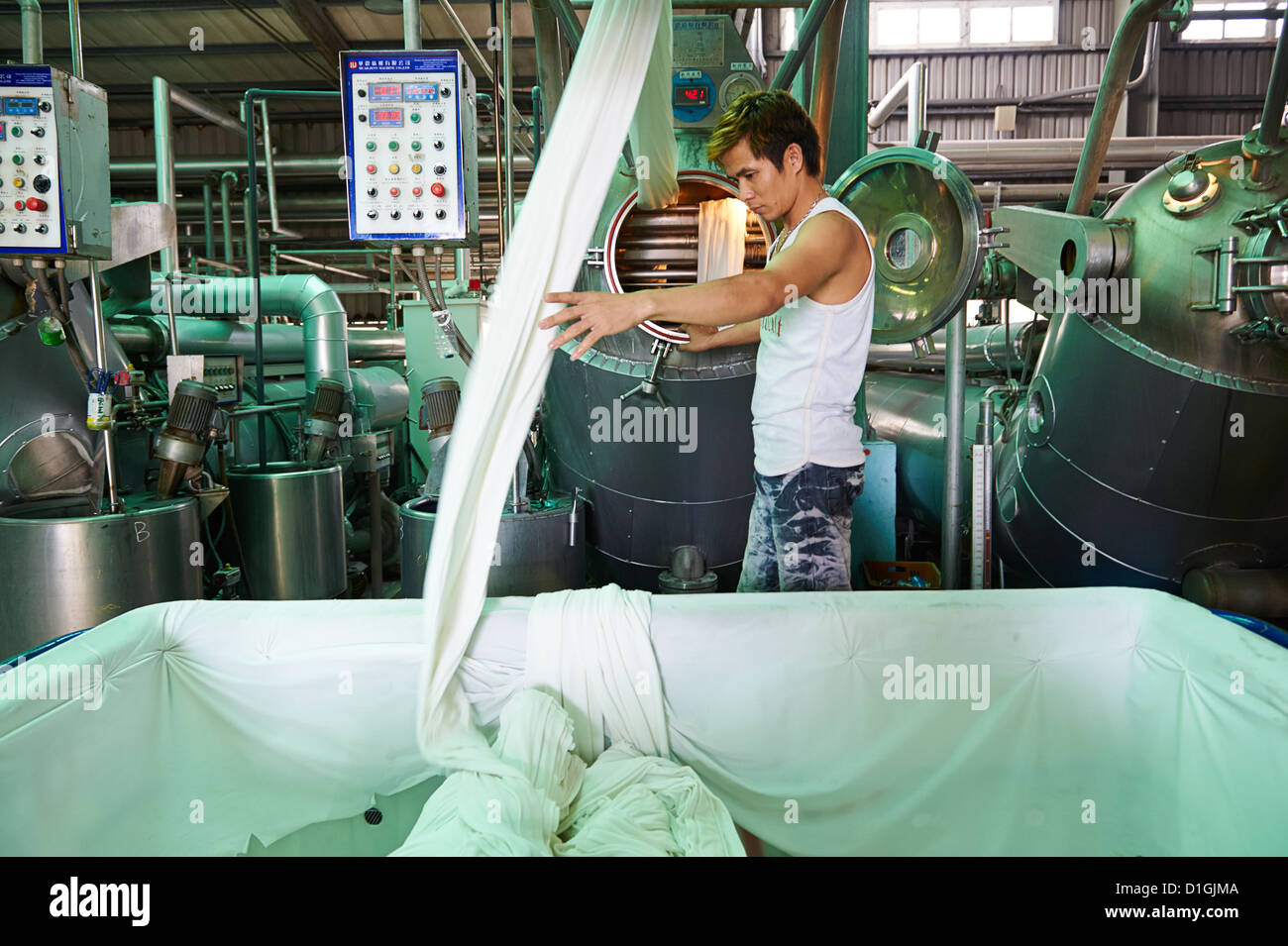 A strong worker poses and inspects fabric next to large dying machines ...