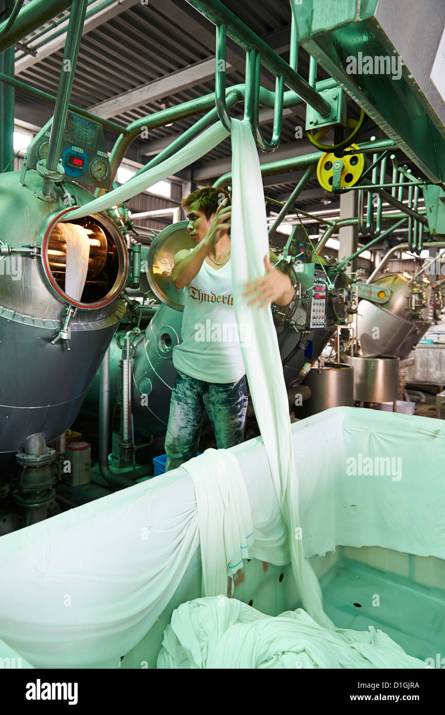 A strong worker poses and inspects fabric next to large dying machines ...