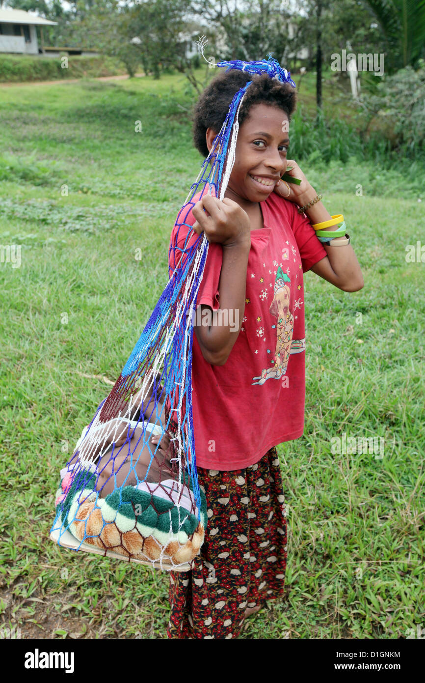 Girl carries her baby sister in a traditional woven bilum hanging from ...