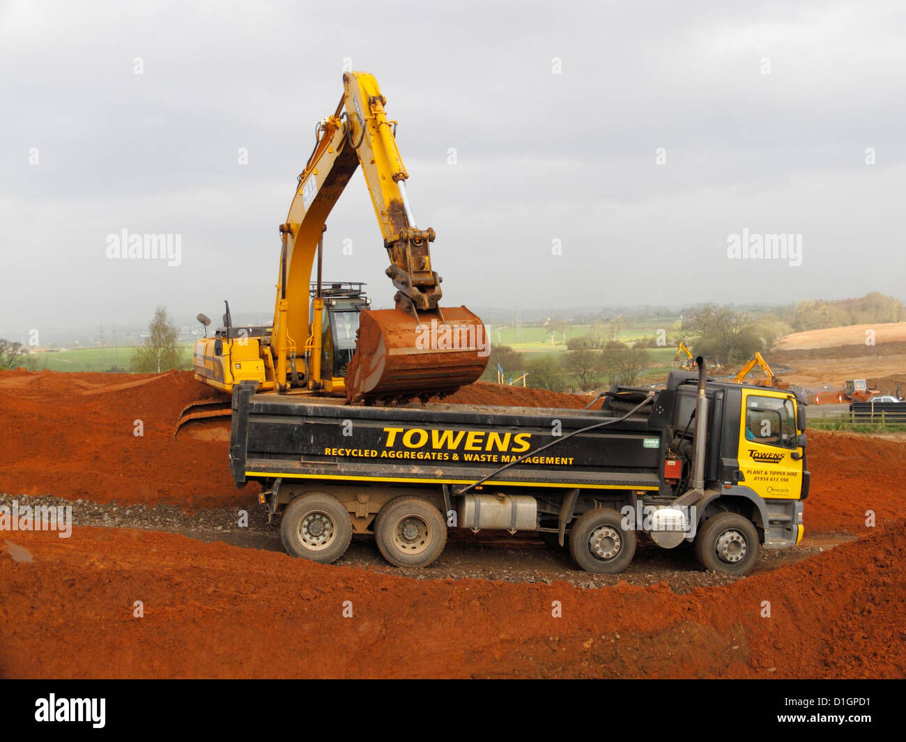 Tracked JCB backhoe excavator loading truck on highway construction ...