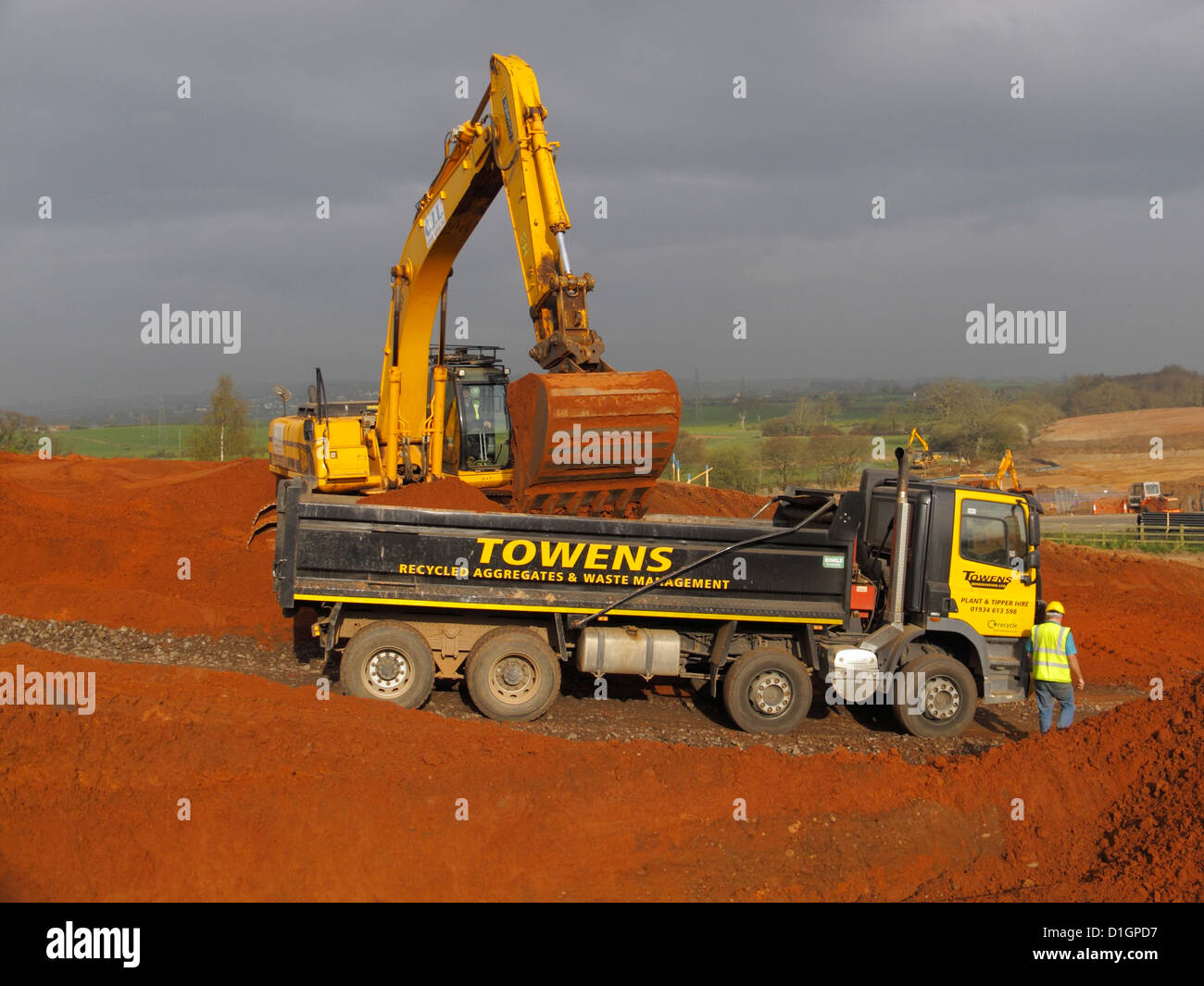Tracked JCB backhoe excavator loading truck on highway construction ...