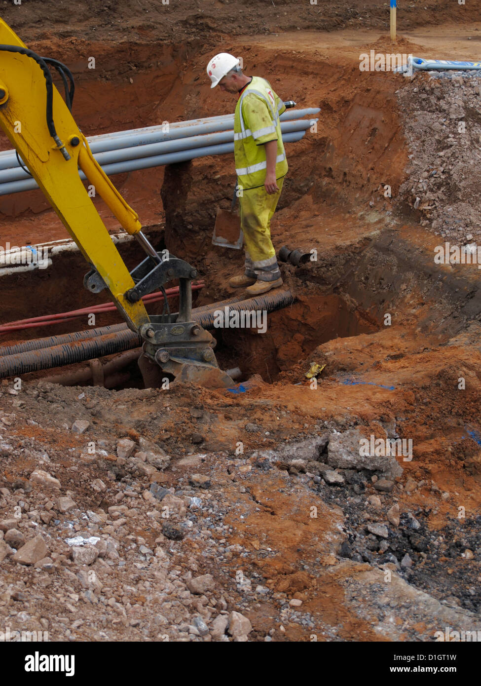 Excavator digging a trench watched by banksman underground utilities ...