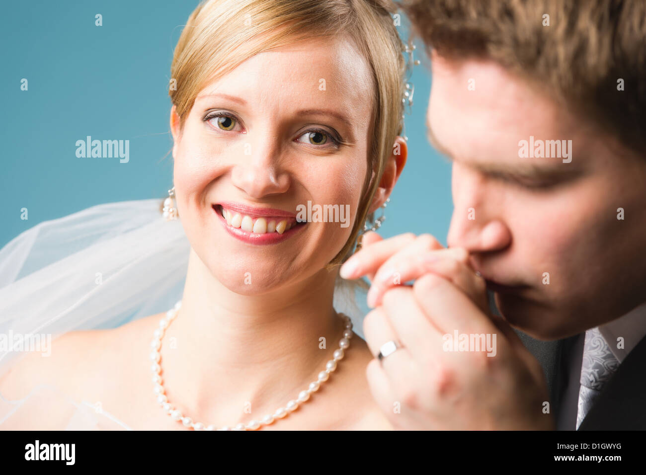 Happy smiling bride, groom kissing hand of the bride, blue background ...
