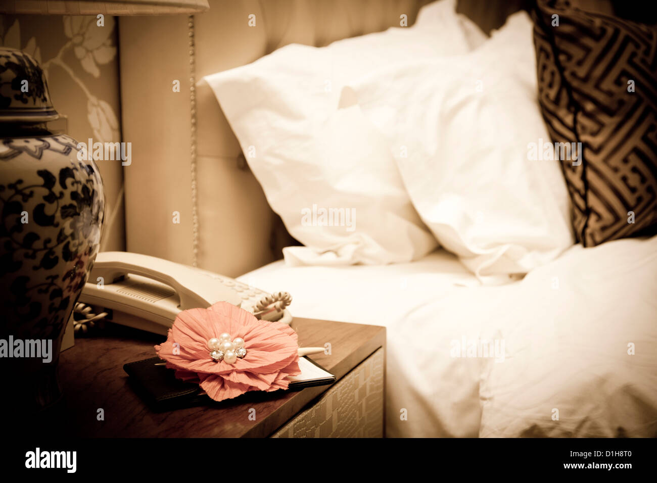 Ornate flower, note pad and telephone on the bed table in hotel room ...