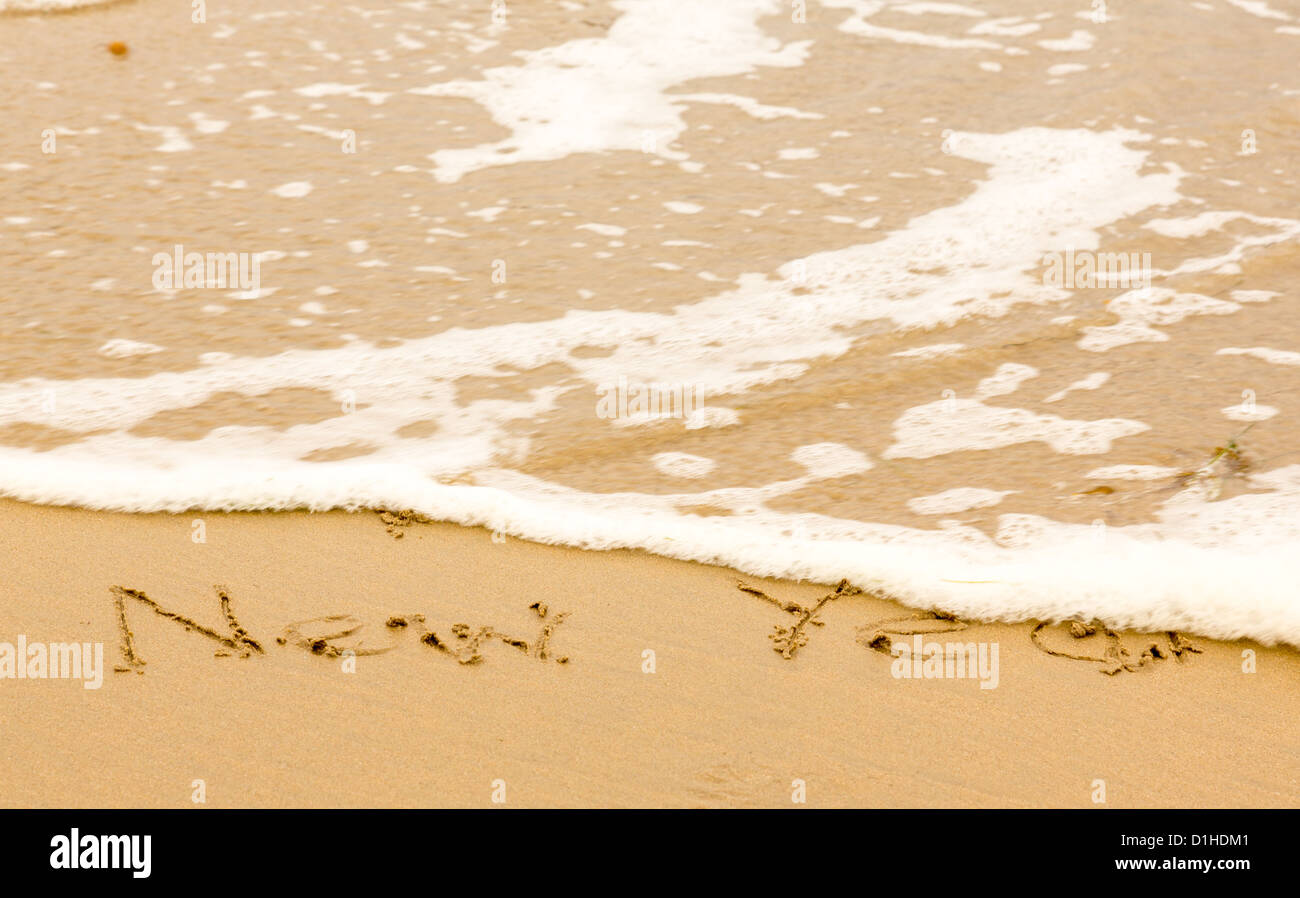 Happy new year sign written in sand on beach with waves approaching ...