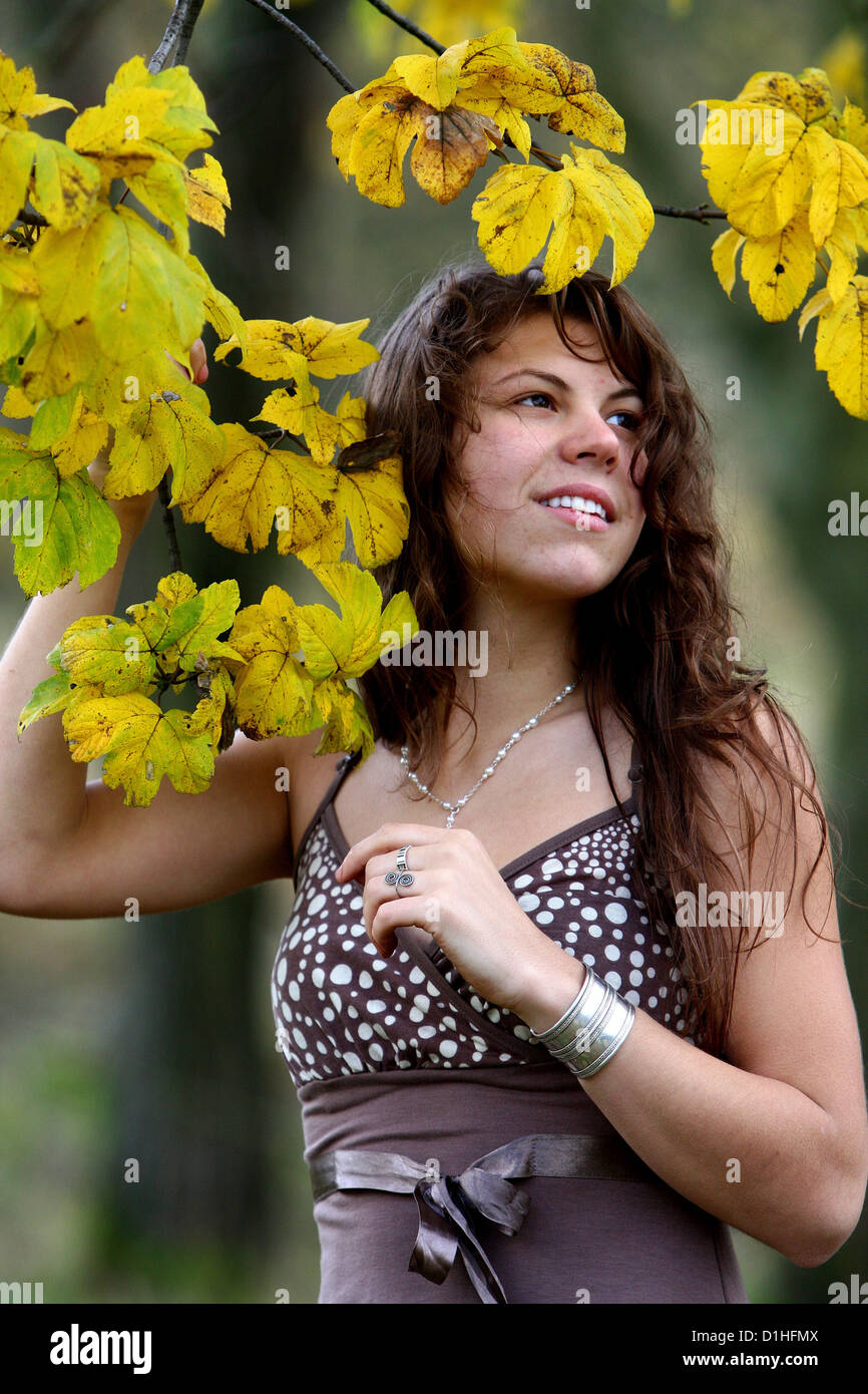 Portrait of a young woman with brown hair under a tree with yellow ...