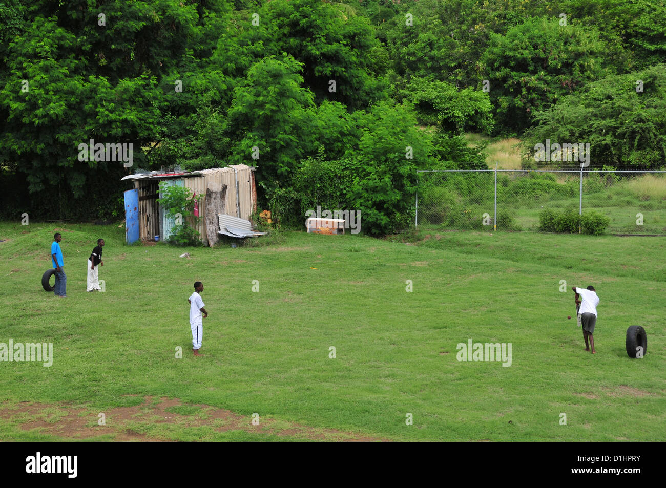 Four West Indian boys playing cricket in casual clothes on grass ...