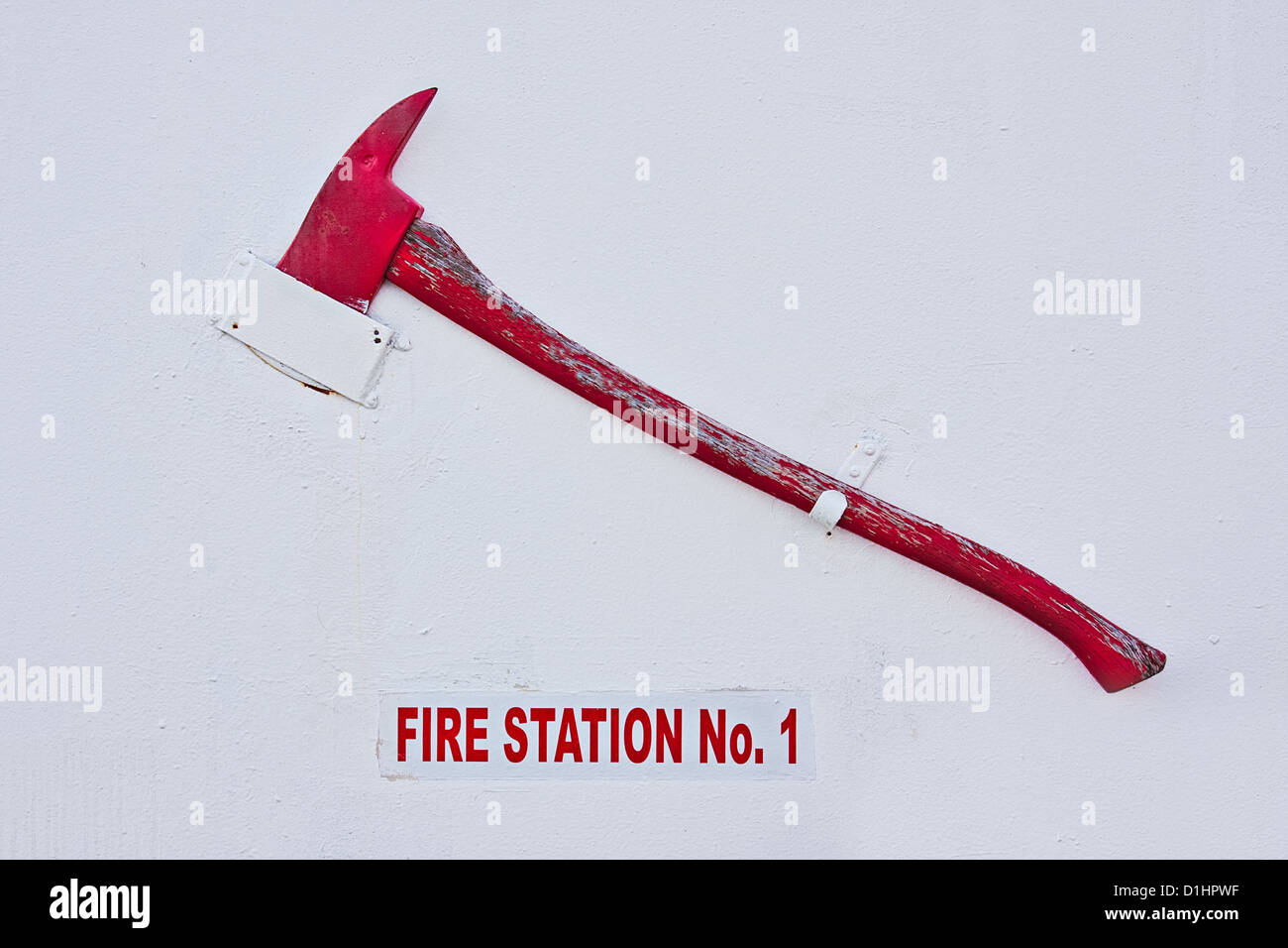A red ax hanging on a white wall of a fire station. There is also a ...