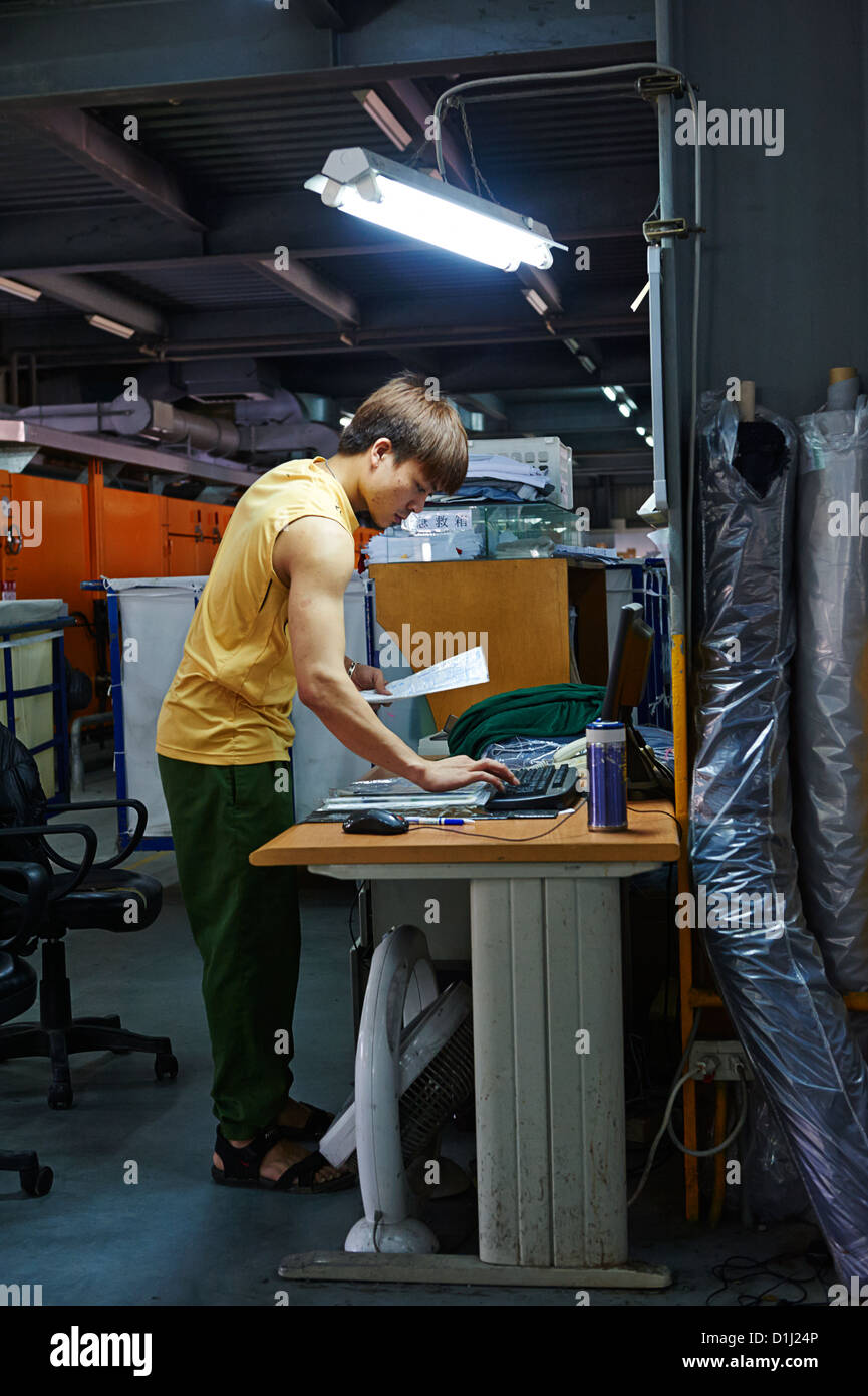 A worker inspects paperwork and enters data into a computer at a ...