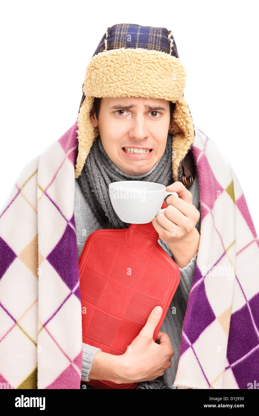 Sick guy covered with blanket holding a hot-water bottle and drinking a ...