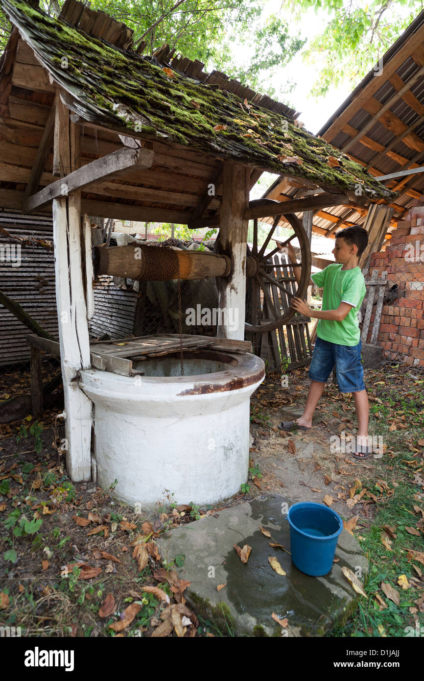 Schoolboy outdoor getting water from a vintage wooden well with pulley ...