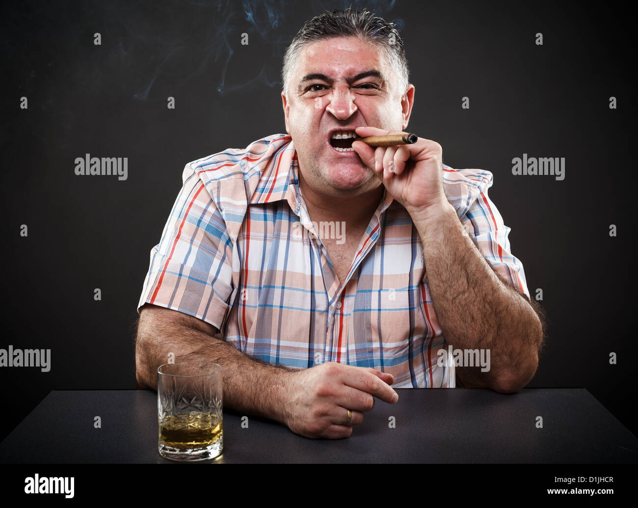 Portrait of a mature mafia man drinking and smoking while sitting at ...