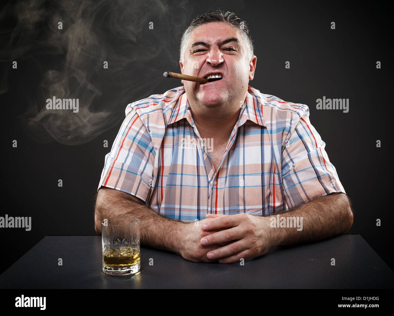 Portrait of a mature mafia man drinking and smoking while sitting at ...