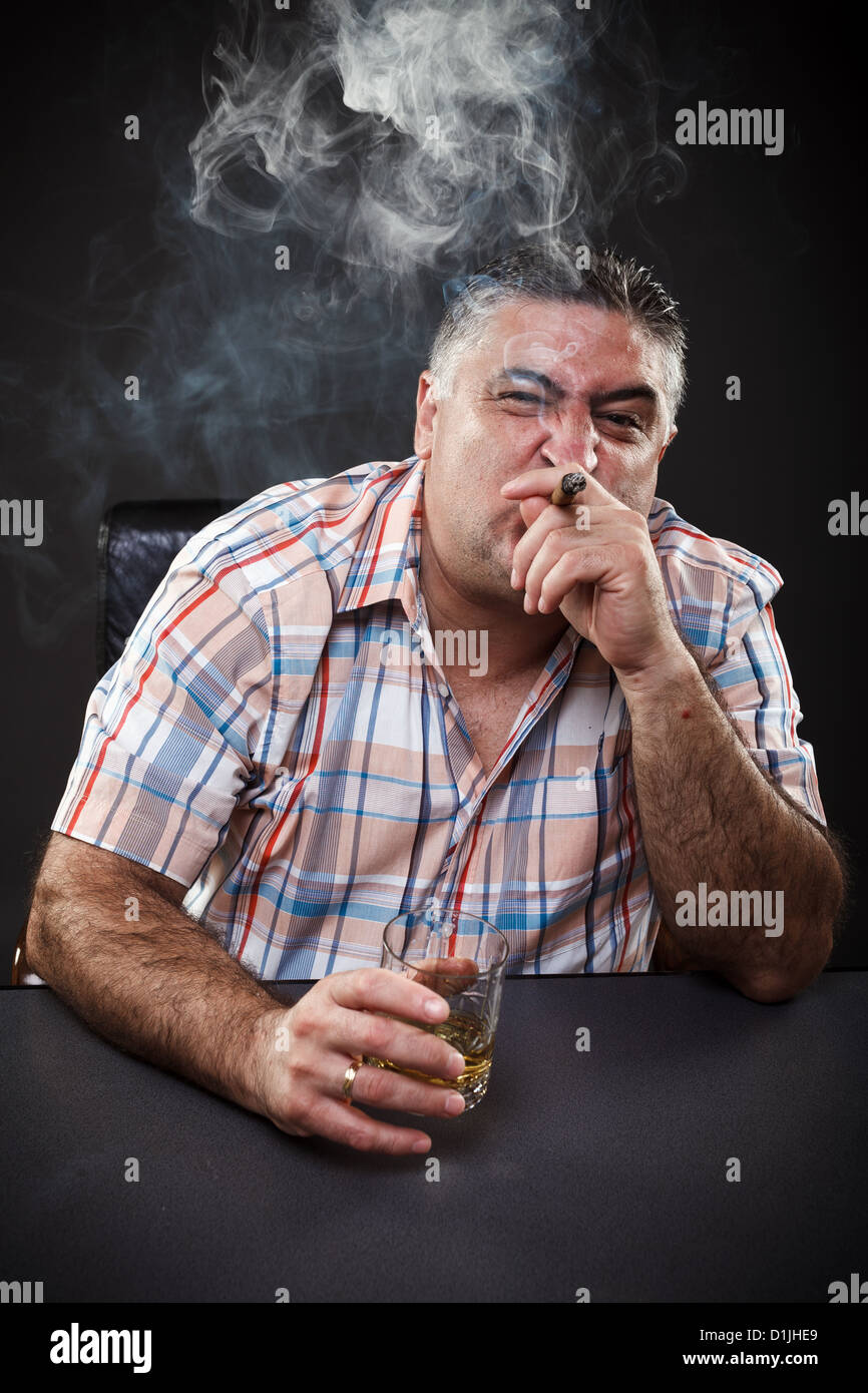 Portrait of a mature mafia man drinking and smoking while sitting at ...