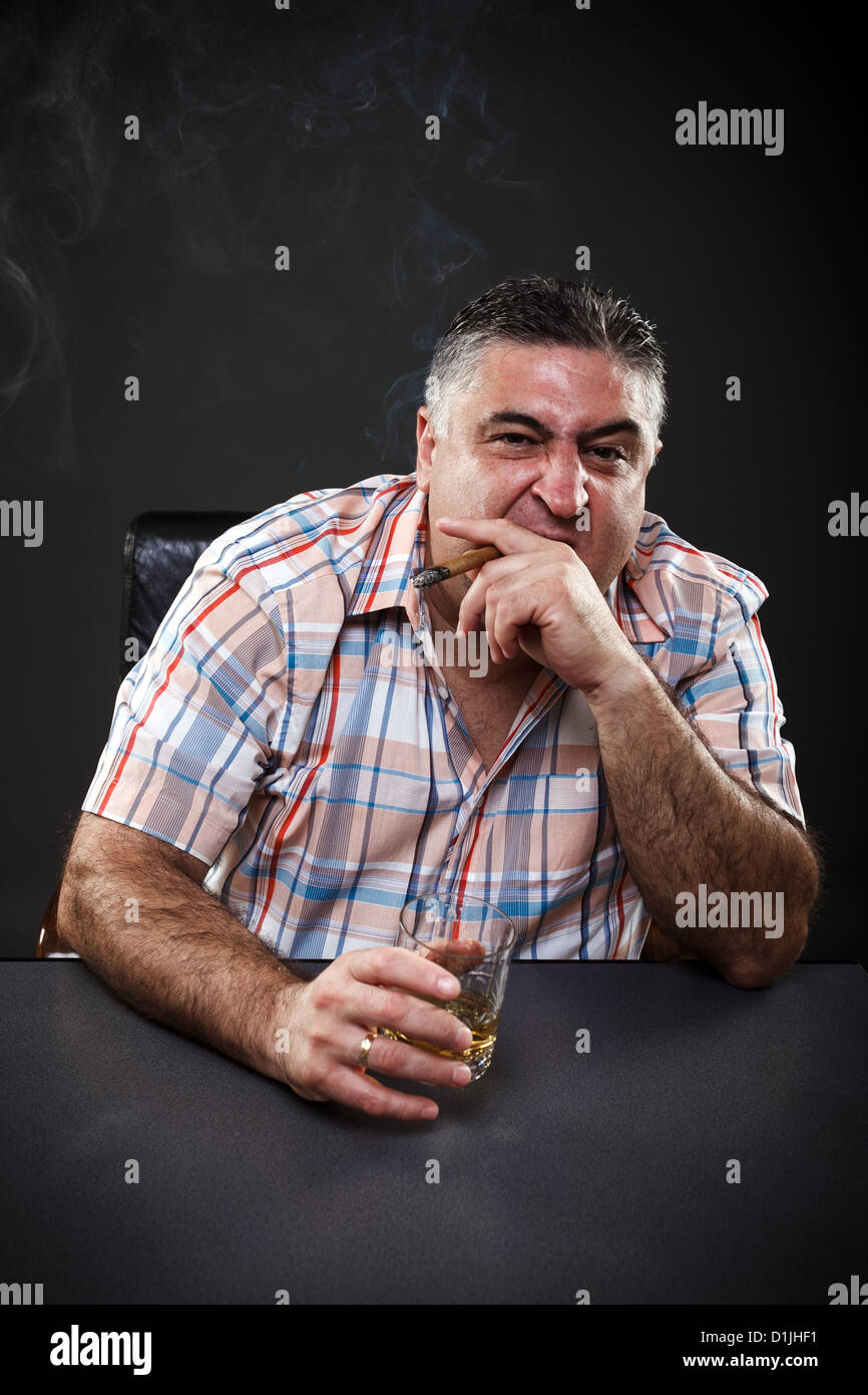 Portrait of a mature mafia man drinking and smoking while sitting at ...