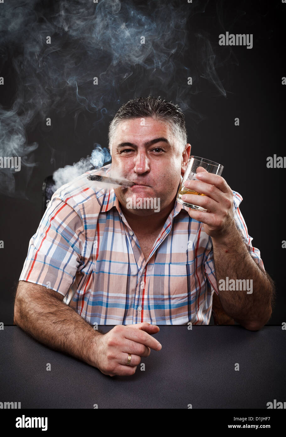 Portrait of a mature mafia man drinking and smoking while sitting at ...