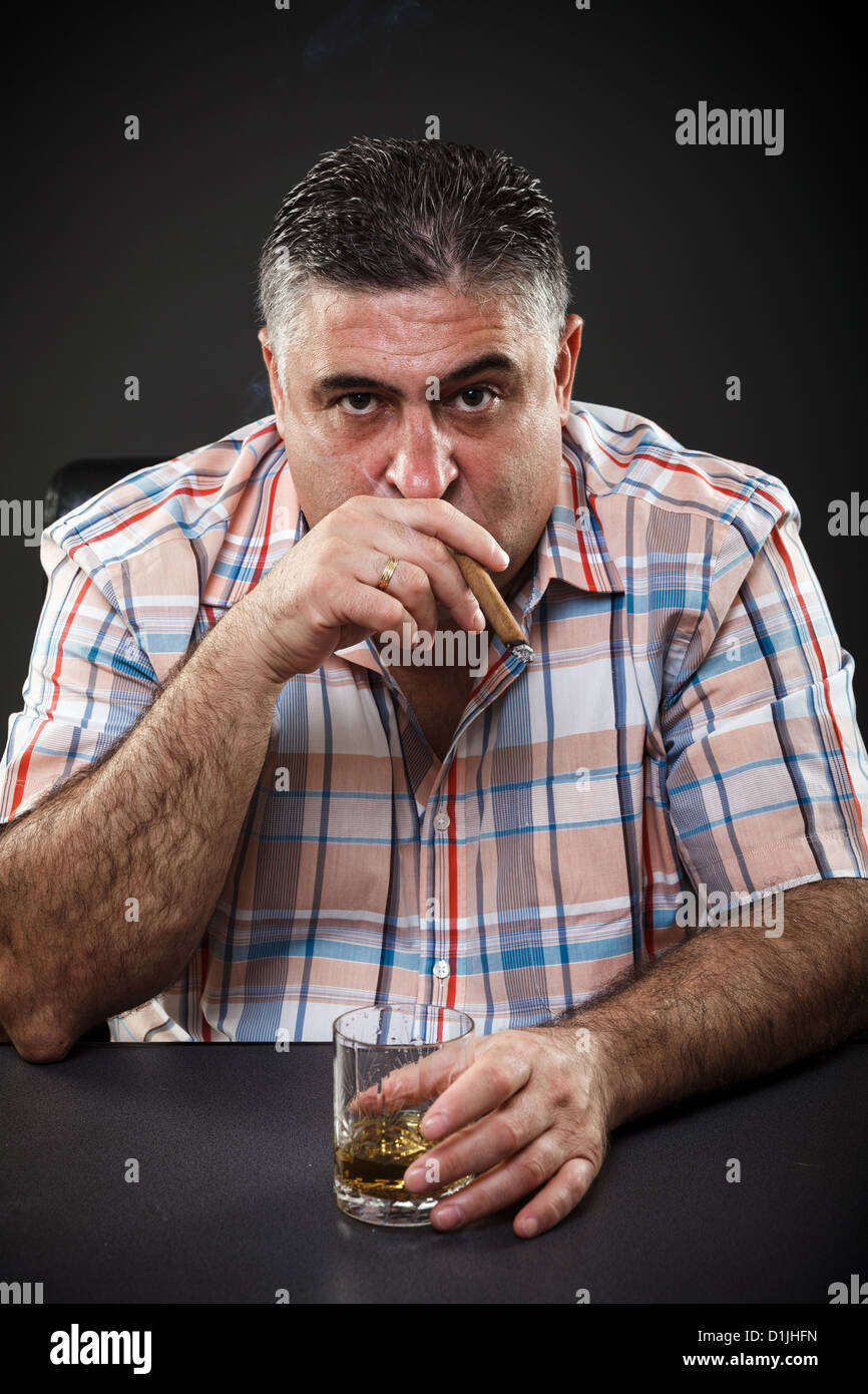 Portrait of a mature mafia man drinking and smoking while sitting at ...