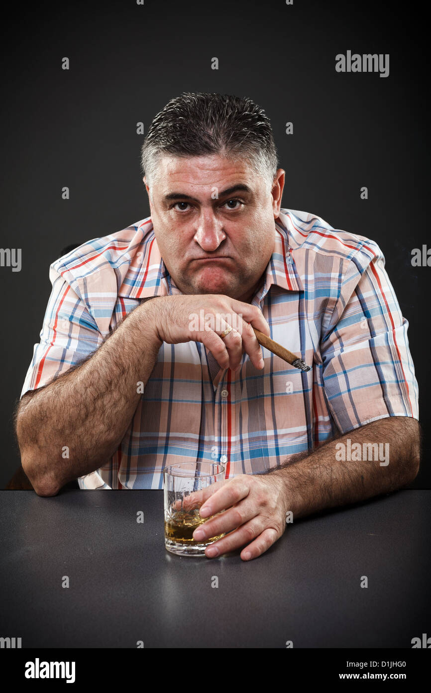 Portrait of a mature mafia man drinking and smoking while sitting at ...