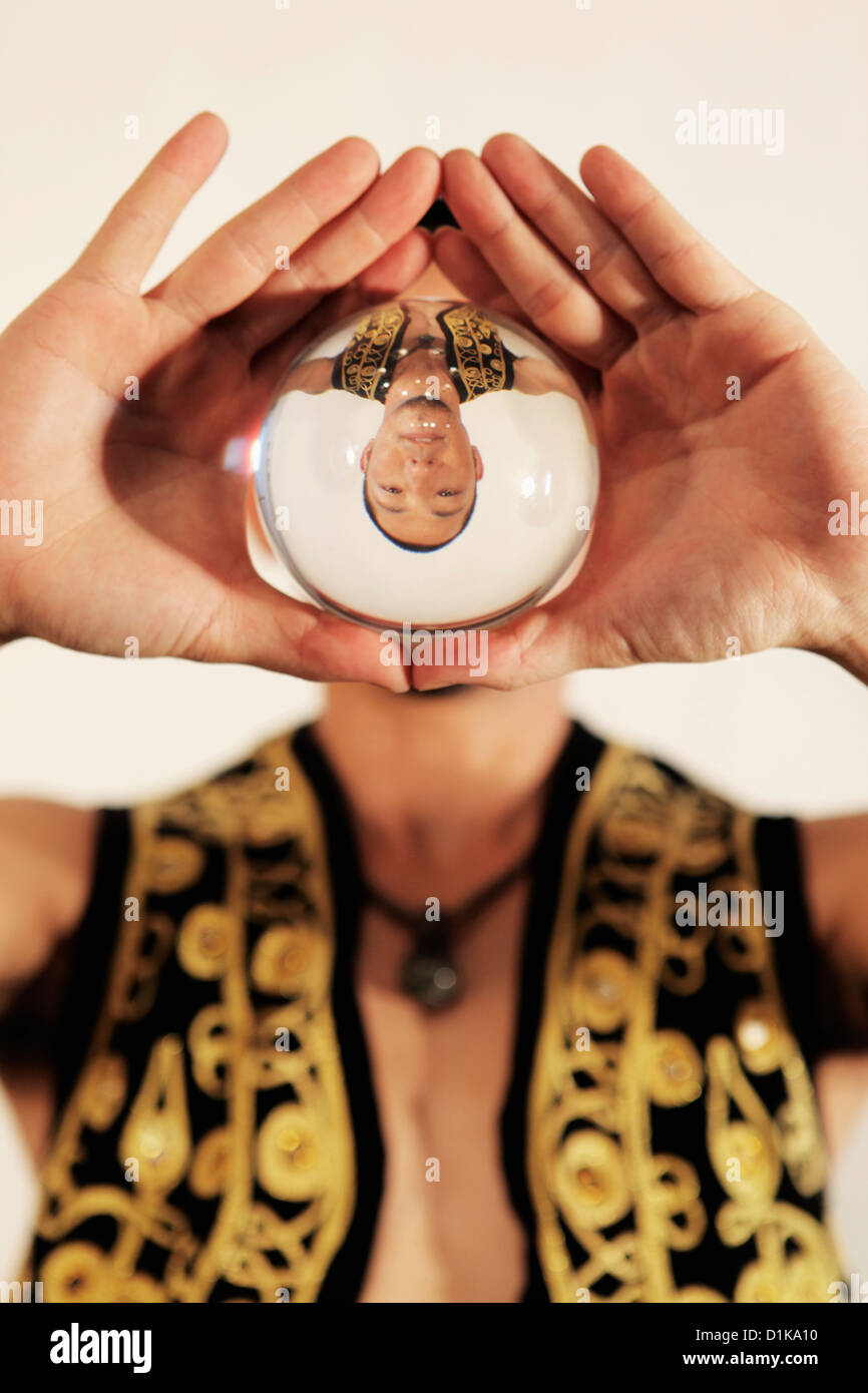 Man holding crystal ball in front of his face with his reflection ...