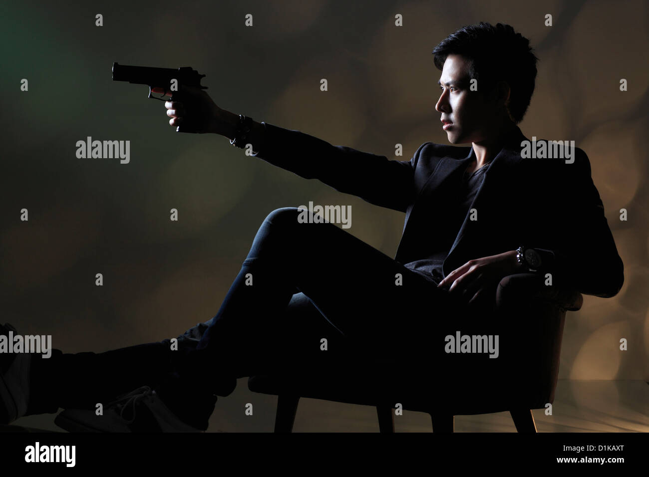 Young man sitting down pointing a gun Stock Photo - Alamy