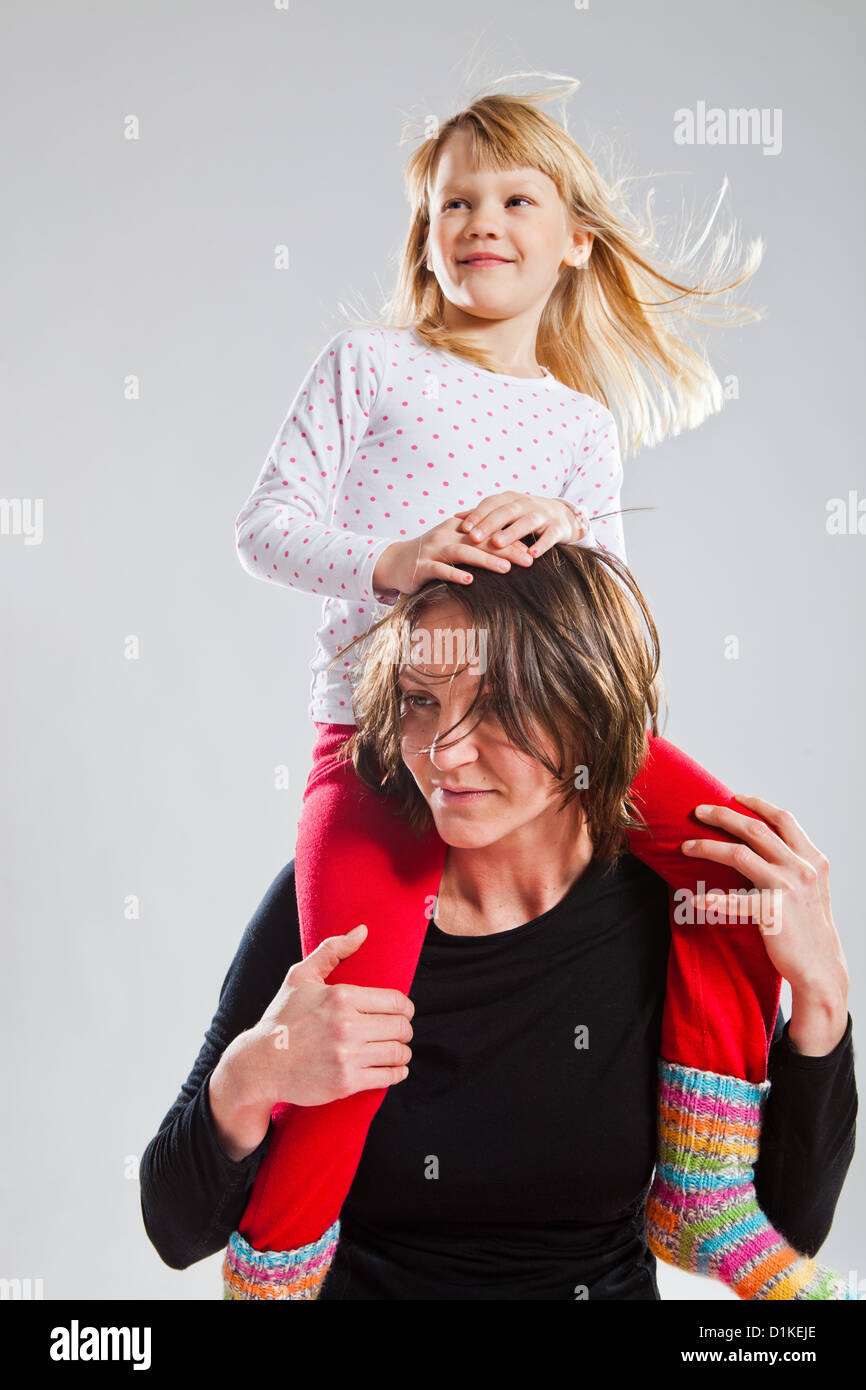 Studio portrait of happy woman carrying smiling young girl on shoulders ...