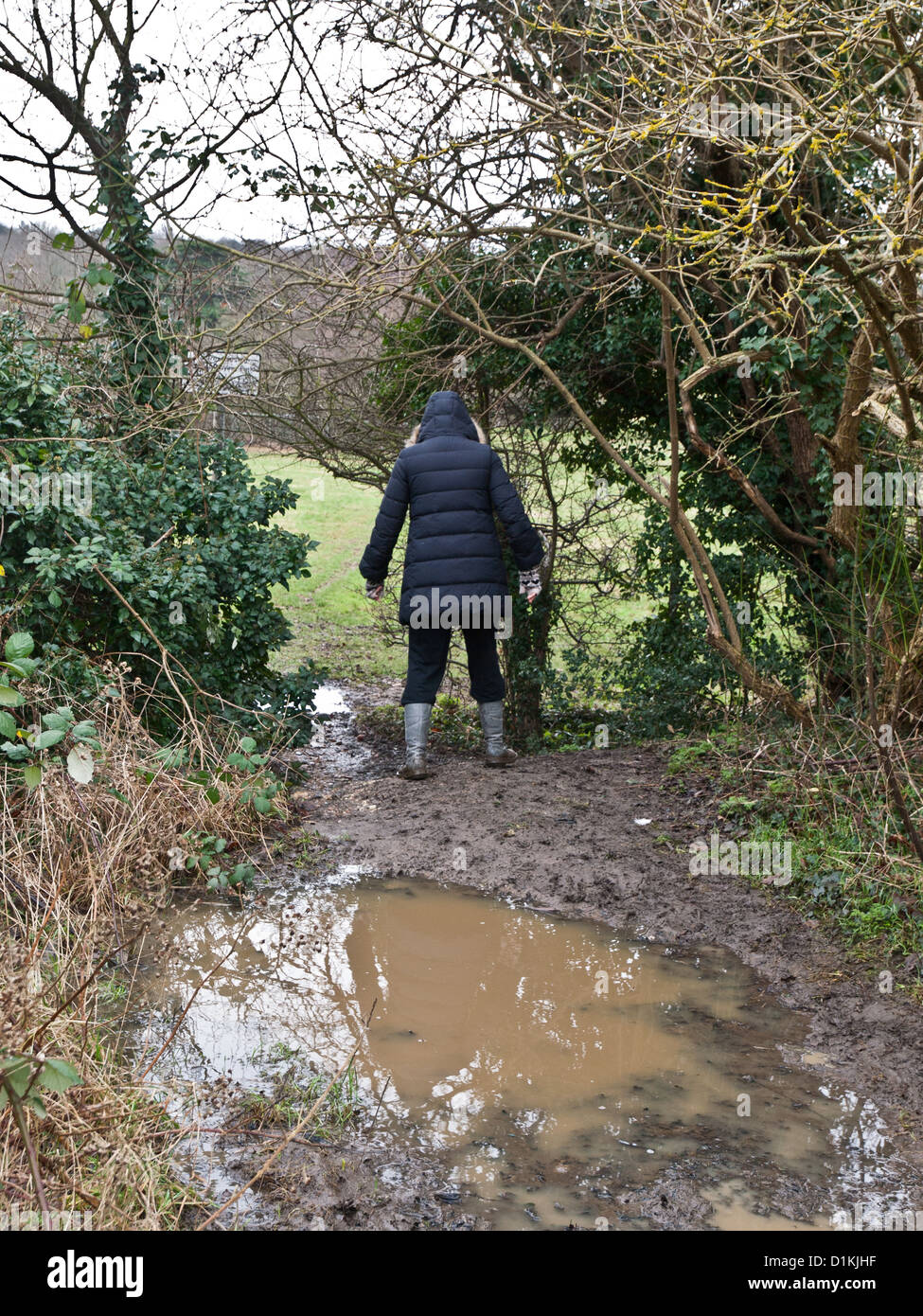 A wrapped up woman attempts to make her way around a muddy puddle ...