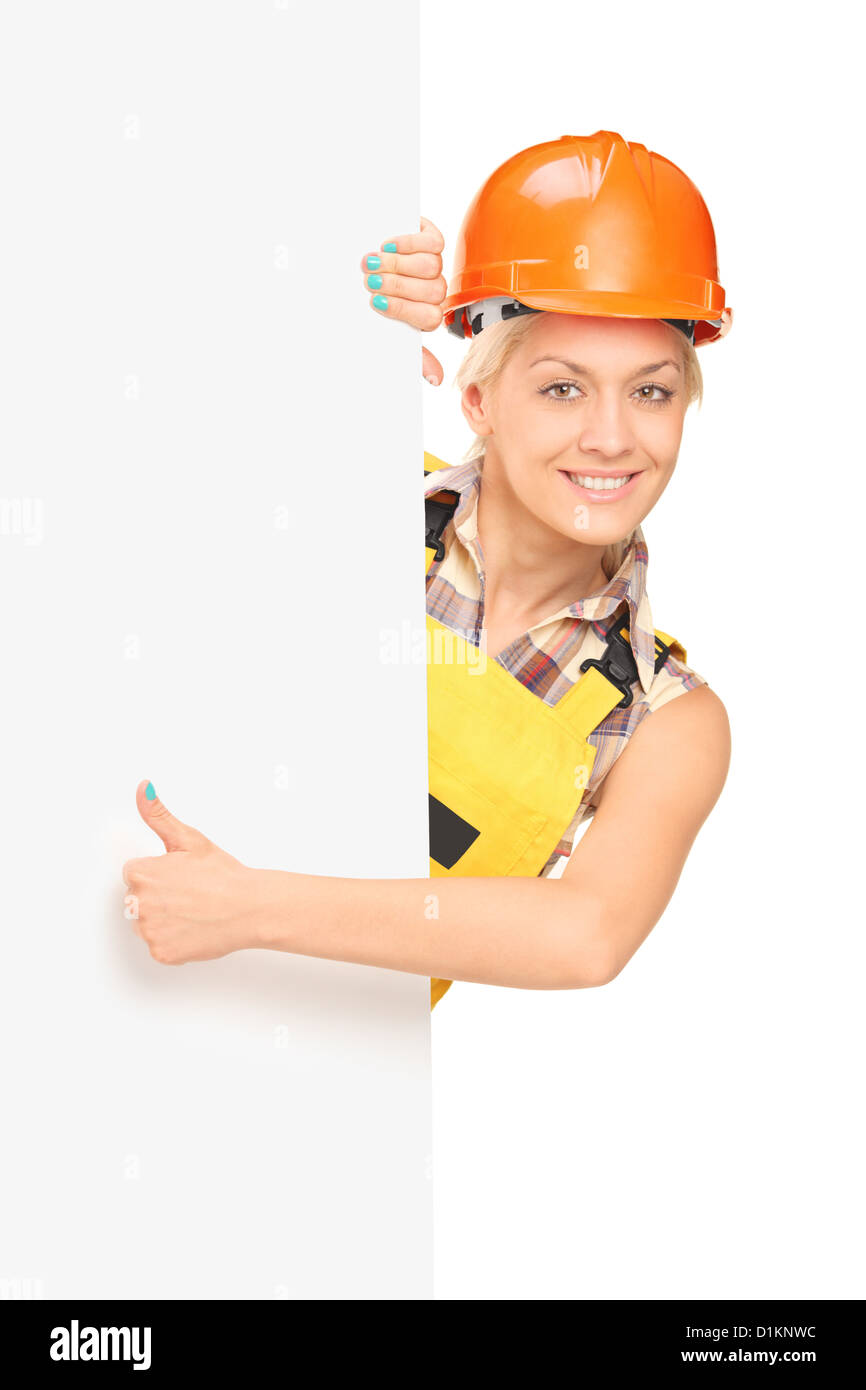 Female manual worker giving a thumb up and standing behind blank panel ...