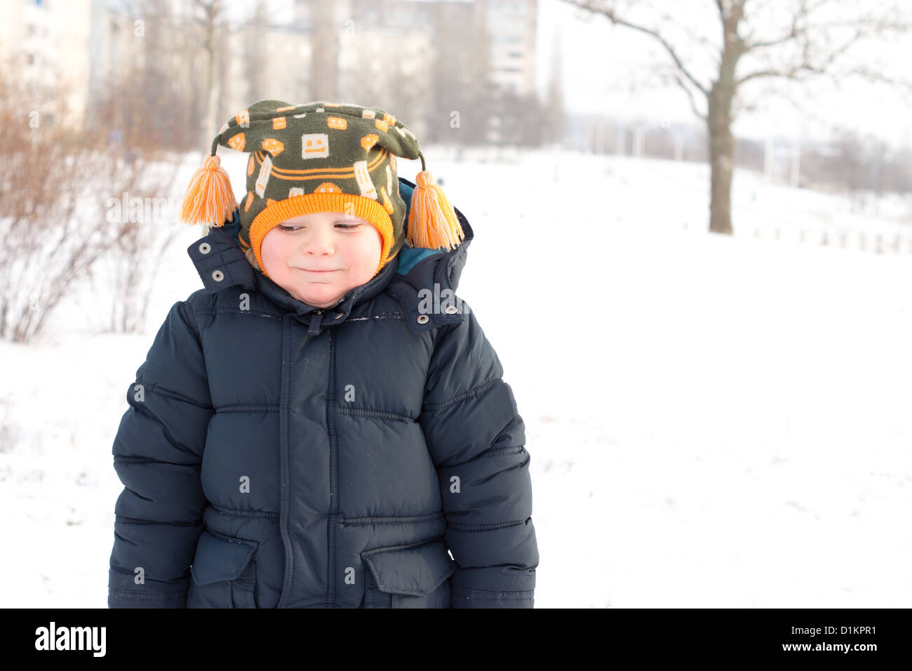 Cold little boy in winter snow giving a cautious smile for the camera ...