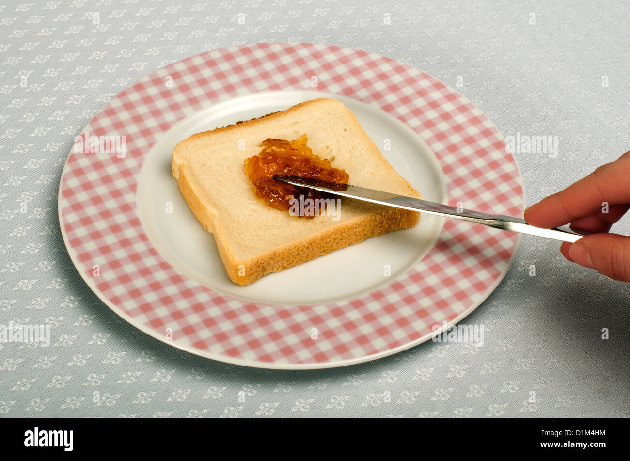 Spread jam on bread with knife. Pink checkered plate Stock Photo - Alamy