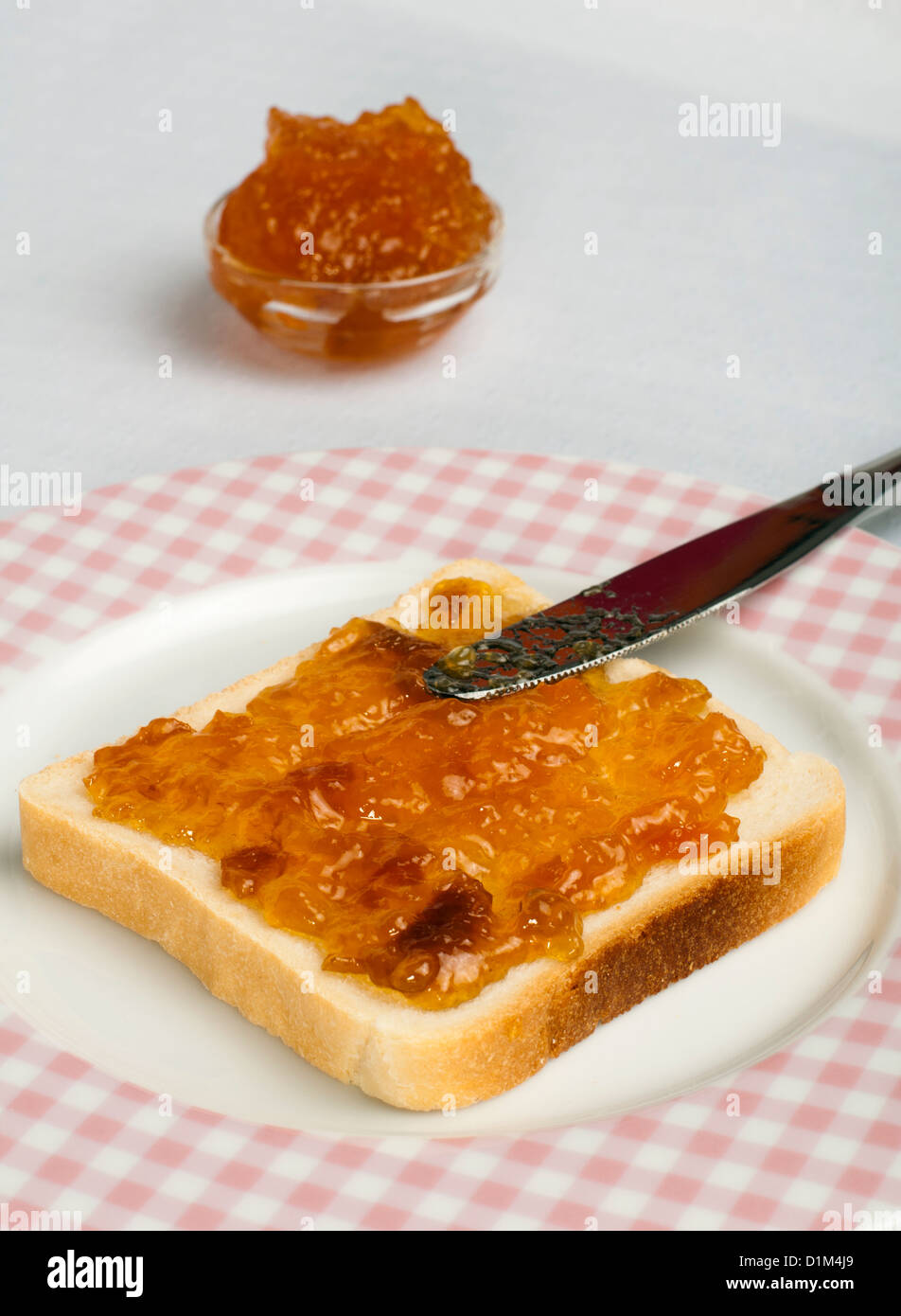 Spread jam on bread with knife. Pink checkered plate Stock Photo - Alamy