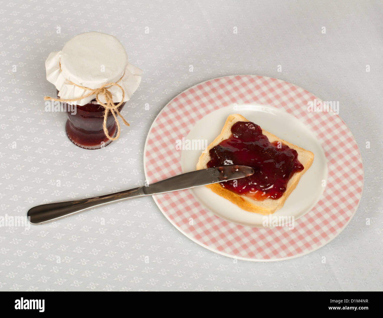 Spread jam on bread with knife and jar of jam. Pink checkered plate ...