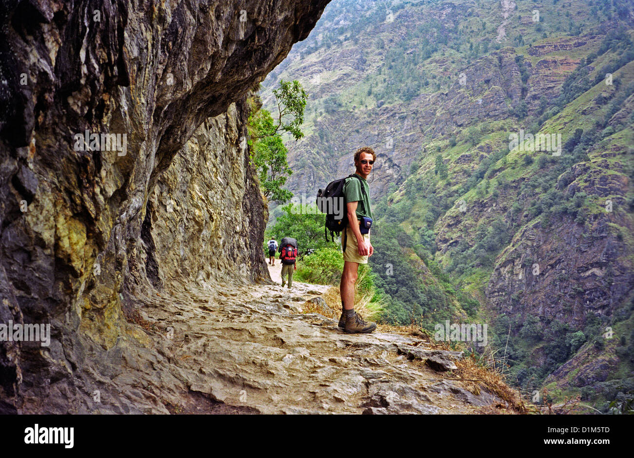 Young man and trekkers carrying rucksacs on path hewn from cliff in ...