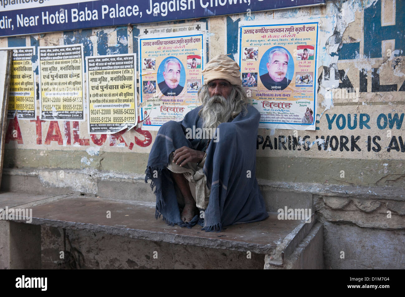 A long haired long bearded Indian beggar sits ona concrete bench in ...