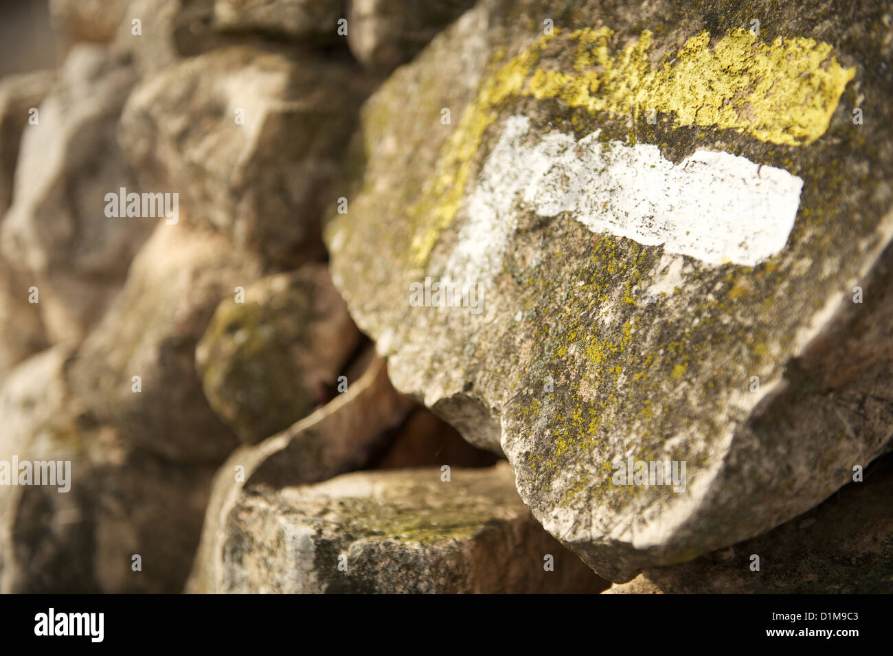 Yellow and white hiking waymarker on stone wall indicating a change in ...