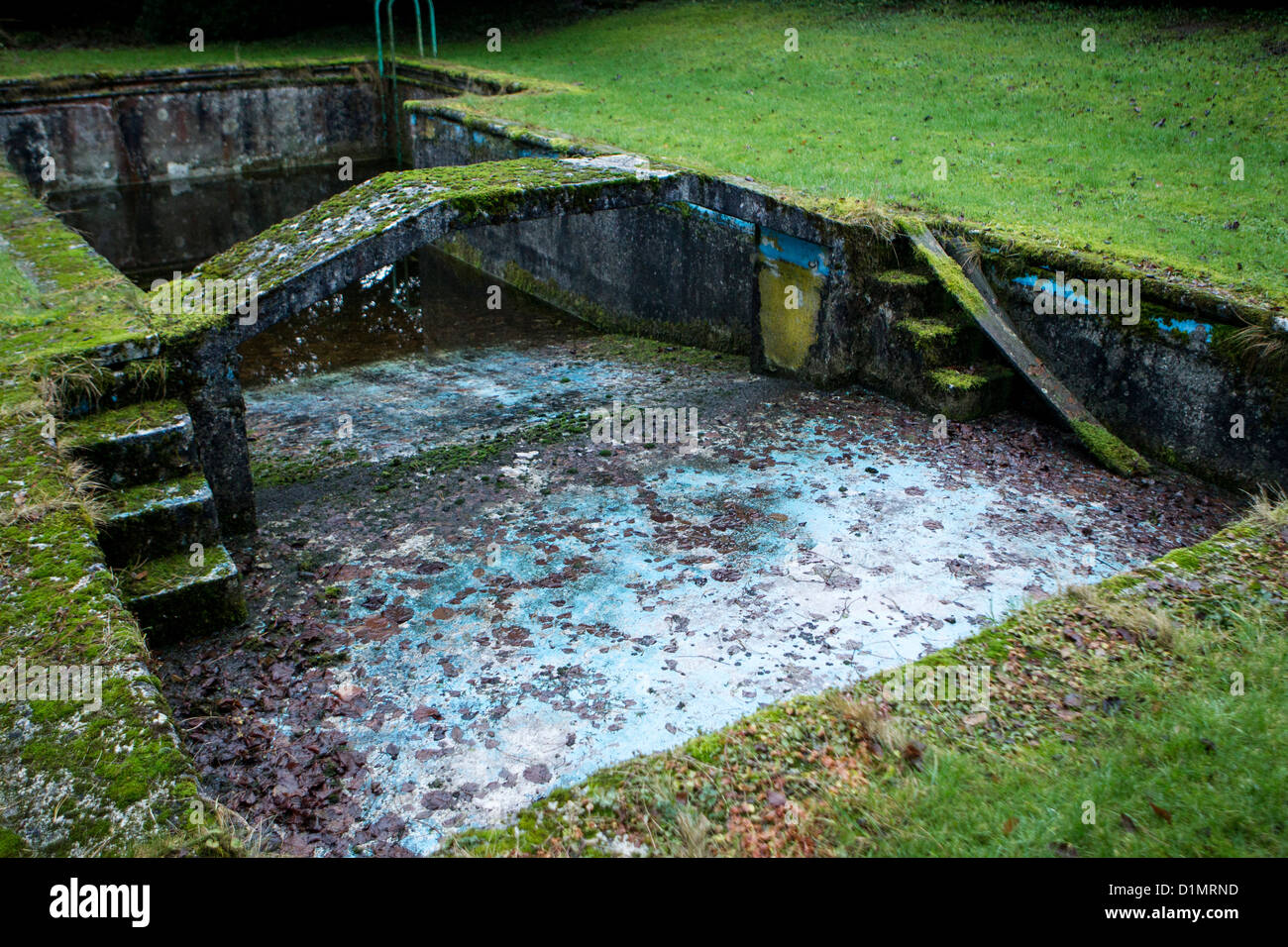 An empty and ruined outdoor swimming pool, covered in moss and ...