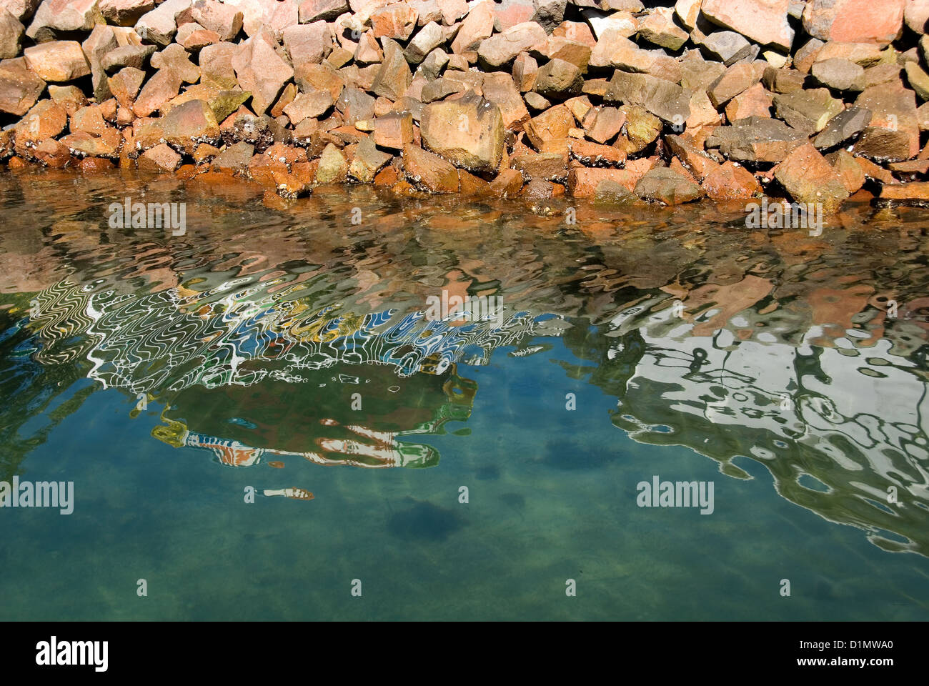 Reflections in the water near a man-made rock breakwater Stock Photo ...