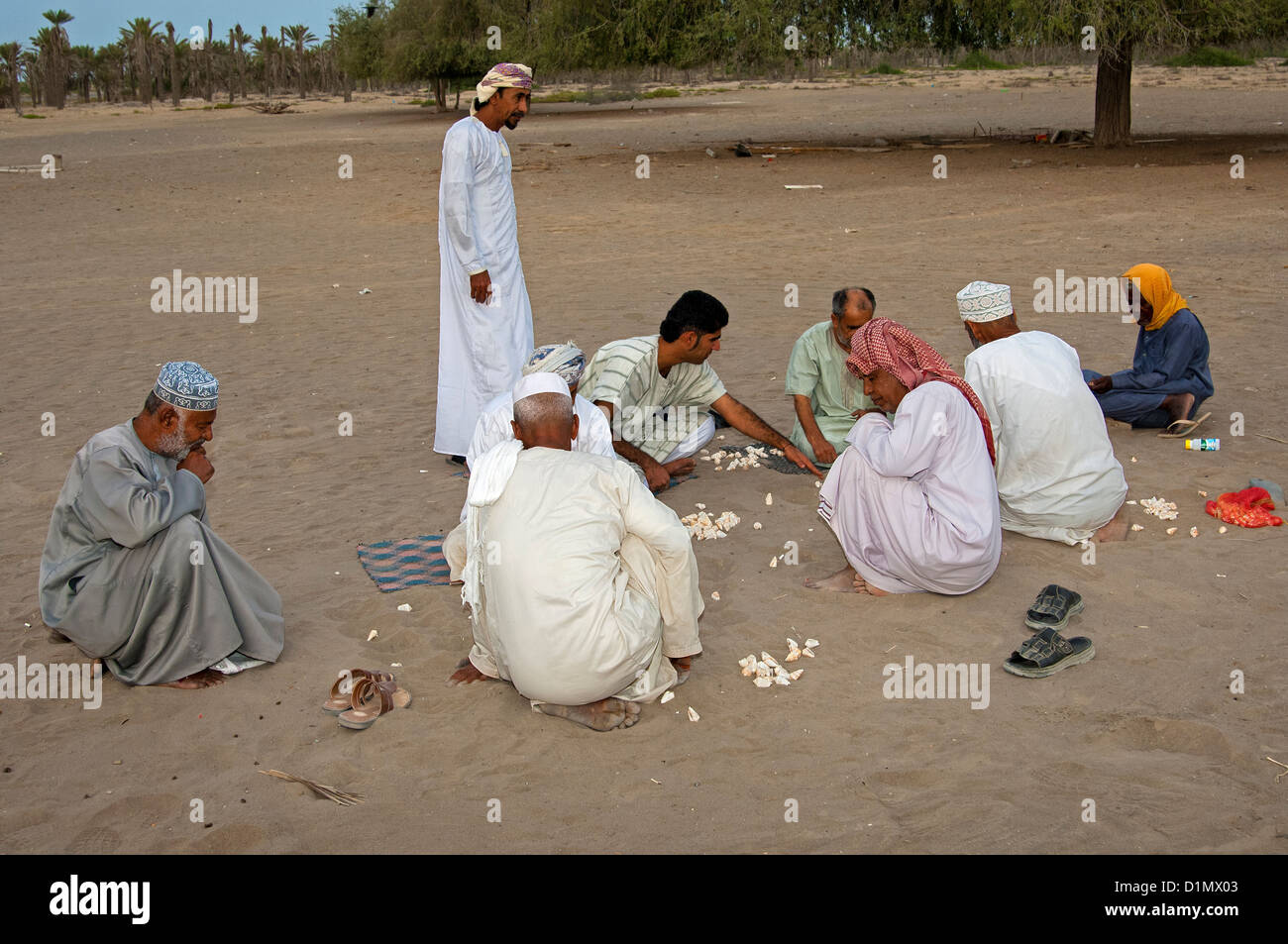 A group of Omani men playing Hawalis with seashells in the sand - the ...