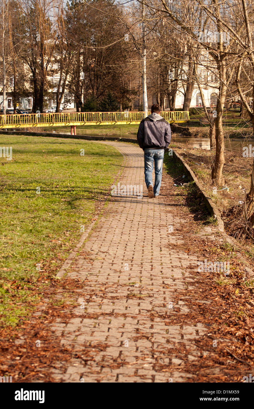 Young man walking through park Stock Photo - Alamy