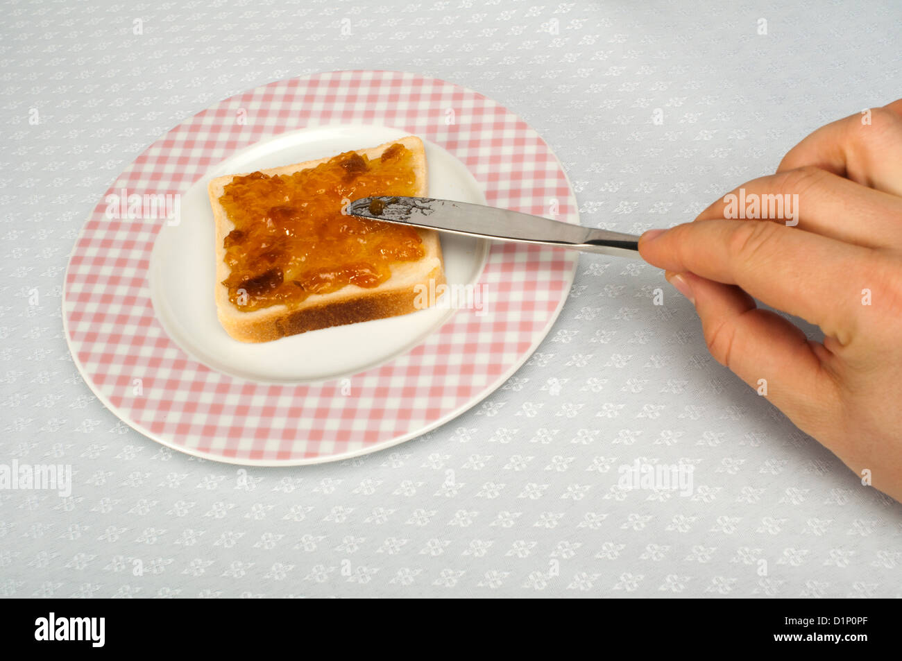 Spread jam on bread with knife. Pink checkered plate Stock Photo - Alamy