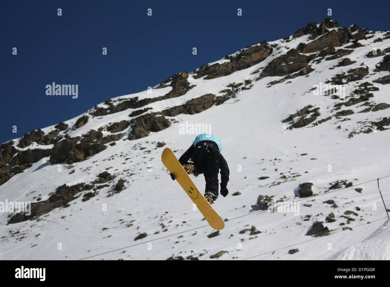 Male snowboarder in mid-air against a mountain backdrop. Snowboard is ...