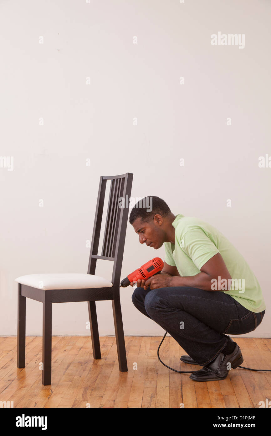 Black man using drill on chair Stock Photo - Alamy