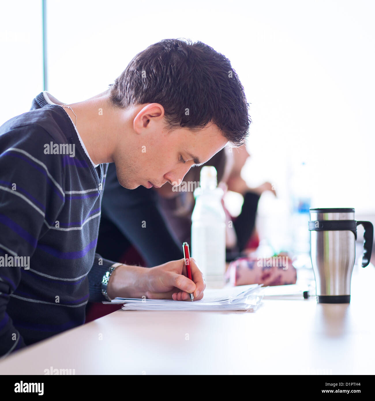 young, handsome male college student sitting in a classroom full of ...