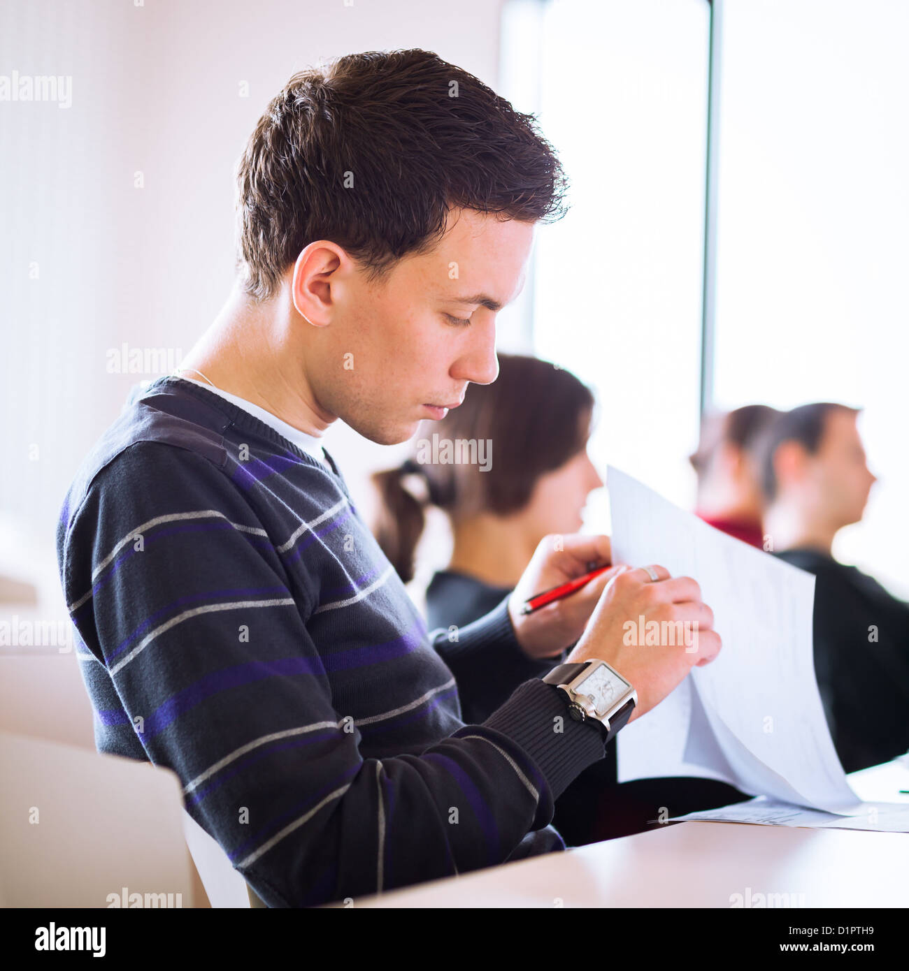 young, handsome male college student sitting in a classroom full of ...